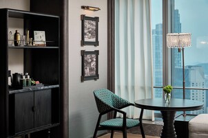 Quarto de hotel moderno com um armário de madeira escura, uma cadeira estampada em verde água, uma mesa redonda com um vaso e quadros nas paredes.