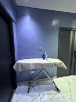 Quarto com parede azul, um painel de passar roupa branco e uma porta.