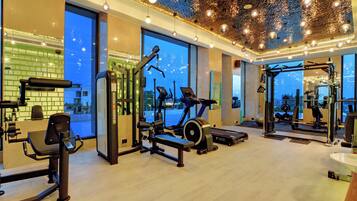 Uma academia moderna com diversos equipamentos de exercício, janelas amplas e um teto com luminárias pendentes.