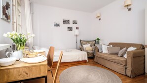 Uma sala de estar moderna com uma mesa de jantar de madeira, um sofá marrom, um tapete redondo e uma cama com colcha branca.