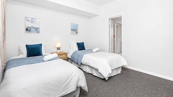 Quarto de hotel com duas camas de solteiro, uma mesinha de cabeceira com abajur, e duas fotos emolduradas na parede.