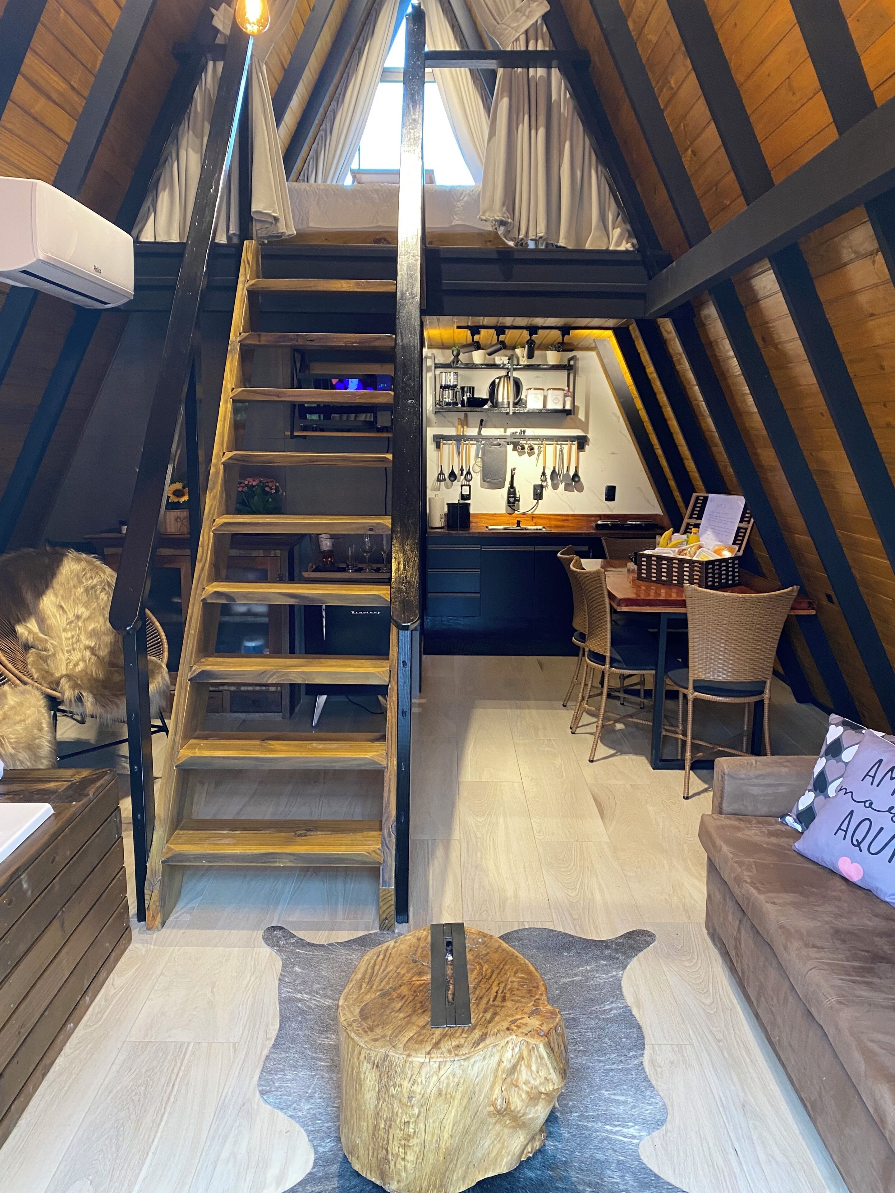 Um quarto de sótão aconchegante com escada de madeira, um espaço de jantar rústico e uma kitchenette.