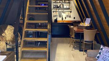 Um quarto de sótão aconchegante com escada de madeira, um espaço de jantar rústico e uma kitchenette.
