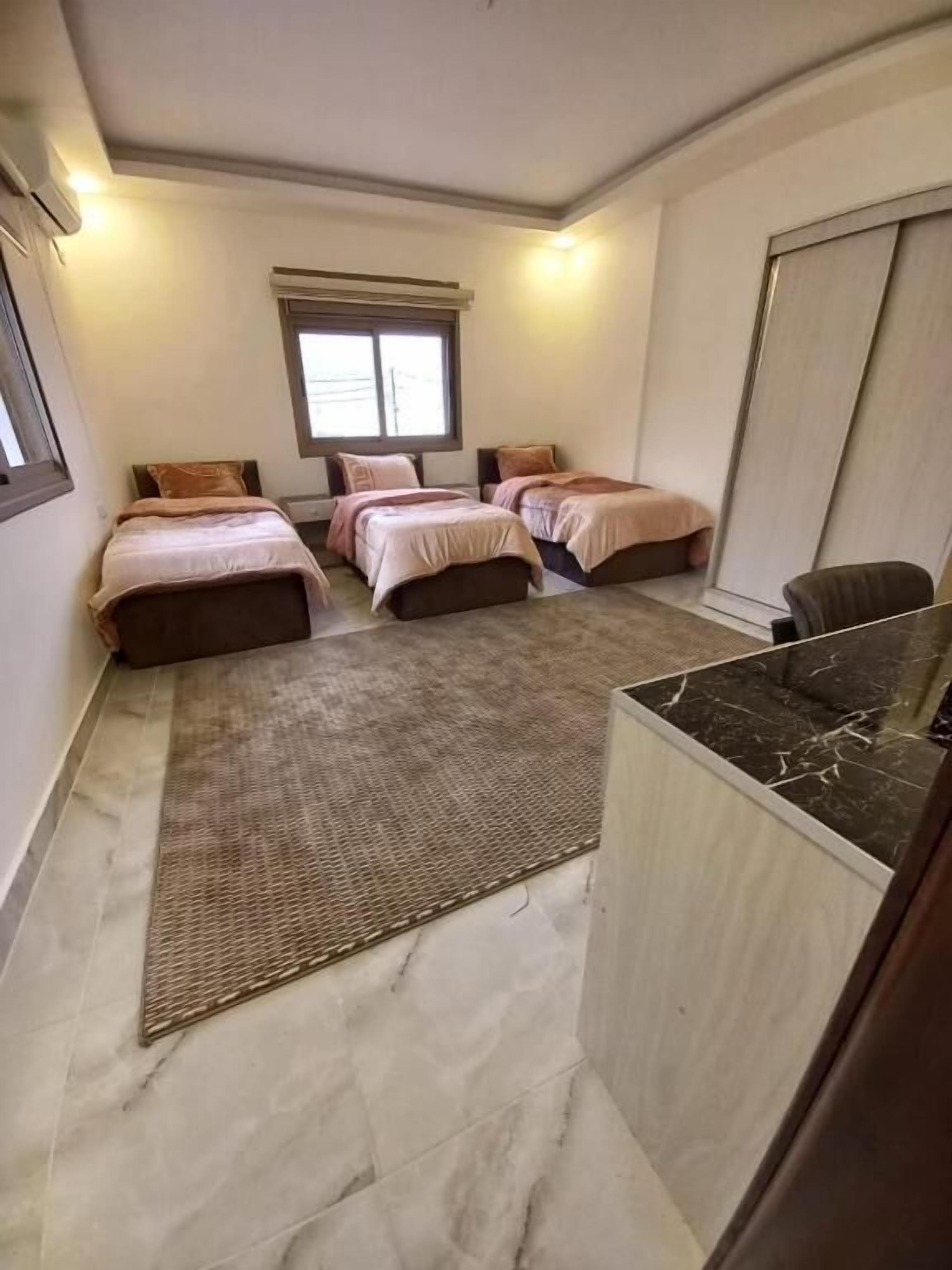 Quarto compacto com três camas, uma pequena mesa e um guarda-roupa espaçoso.