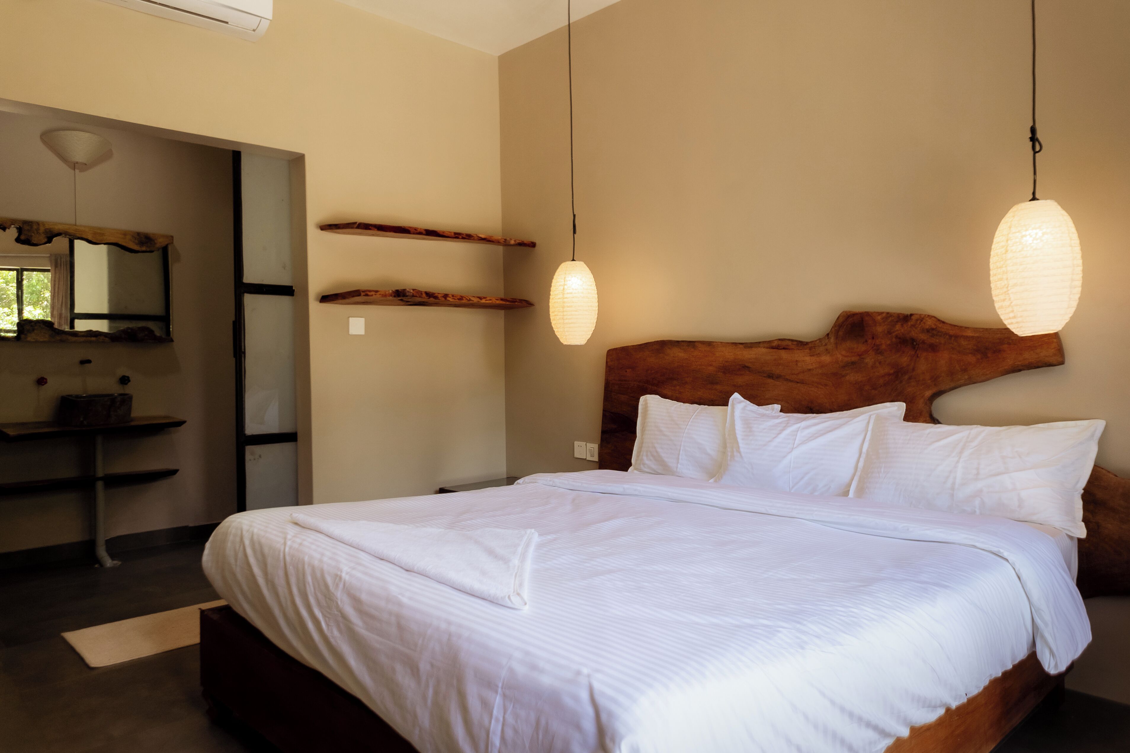 Cama bem arrumada com lençóis brancos, cabeceira de madeira e duas luminárias pendentes.