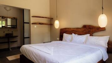 Cama bem arrumada com lençóis brancos, cabeceira de madeira e duas luminárias pendentes.