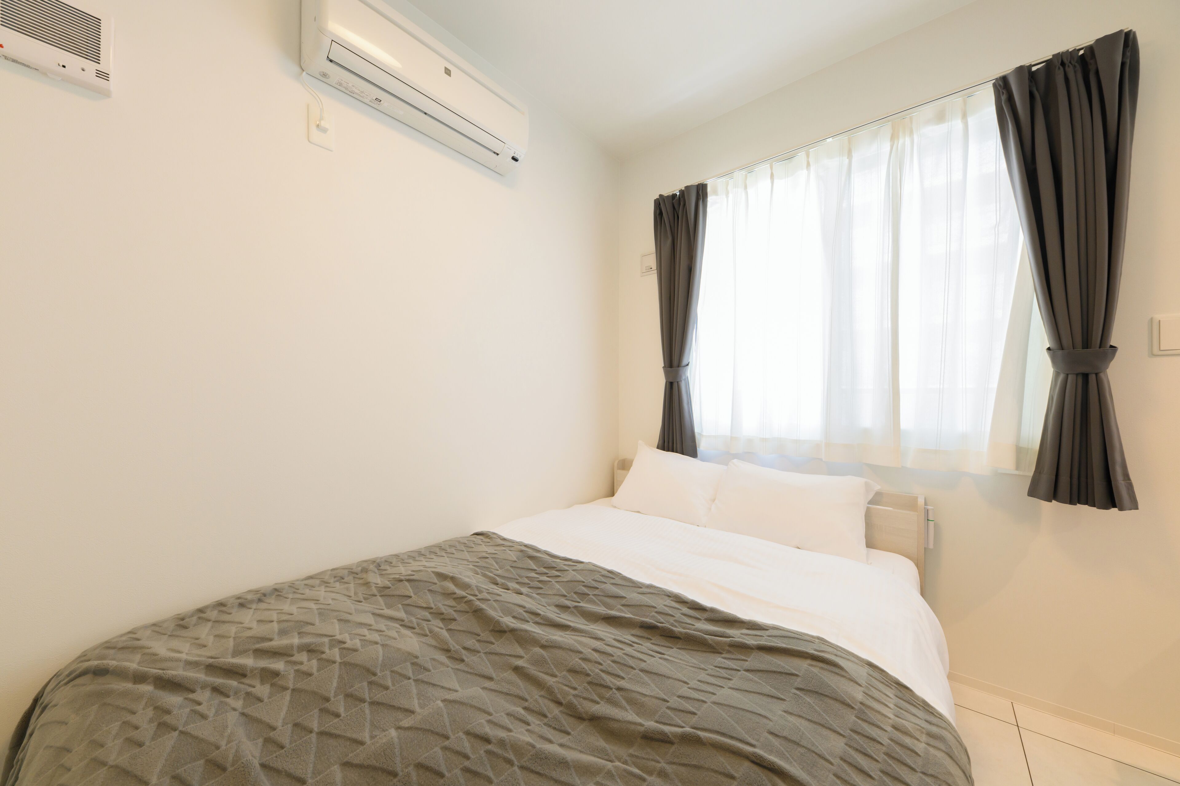 Quarto com cama, janela com cortinas, unidade de ar condicionado e interruptor de luz na parede.