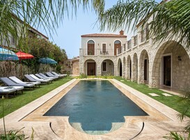 Uma área de piscina com espreguiçadeiras e um edifício de pedra com arcos.