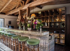 Uma área de bar com bancada de mármore, banquetes verdes e diversos arranjos florais e copos.