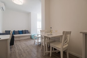 Um espaço de estar moderno com área de jantar, sofá com almofadas e piso em tons claros.