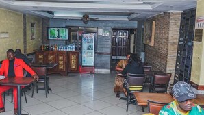 Restaurante com área de bar, piso ladrilhado e uma televisão exibindo uma partida esportiva.