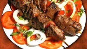 Um prato de espetinhos de carne grelhada com tomates e cebolas.