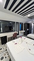 Quarto de hotel com cama, escrivaninha, cadeira, espelho e televisão.