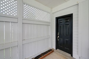 Uma porta de madeira branca com um painel preto, cerca branca de piquete e um degrau de concreto que leva à porta.