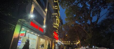 Hotel com letreiro de neon, mesas ao ar livre e vista para a rua.