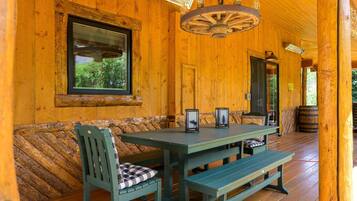 Interior de uma cabana de madeira com mesa, bancos e janela com vista para o verde.