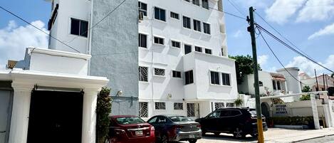 Um hotel com vários andares, fachada branca, diversas varandas e entrada com portão.