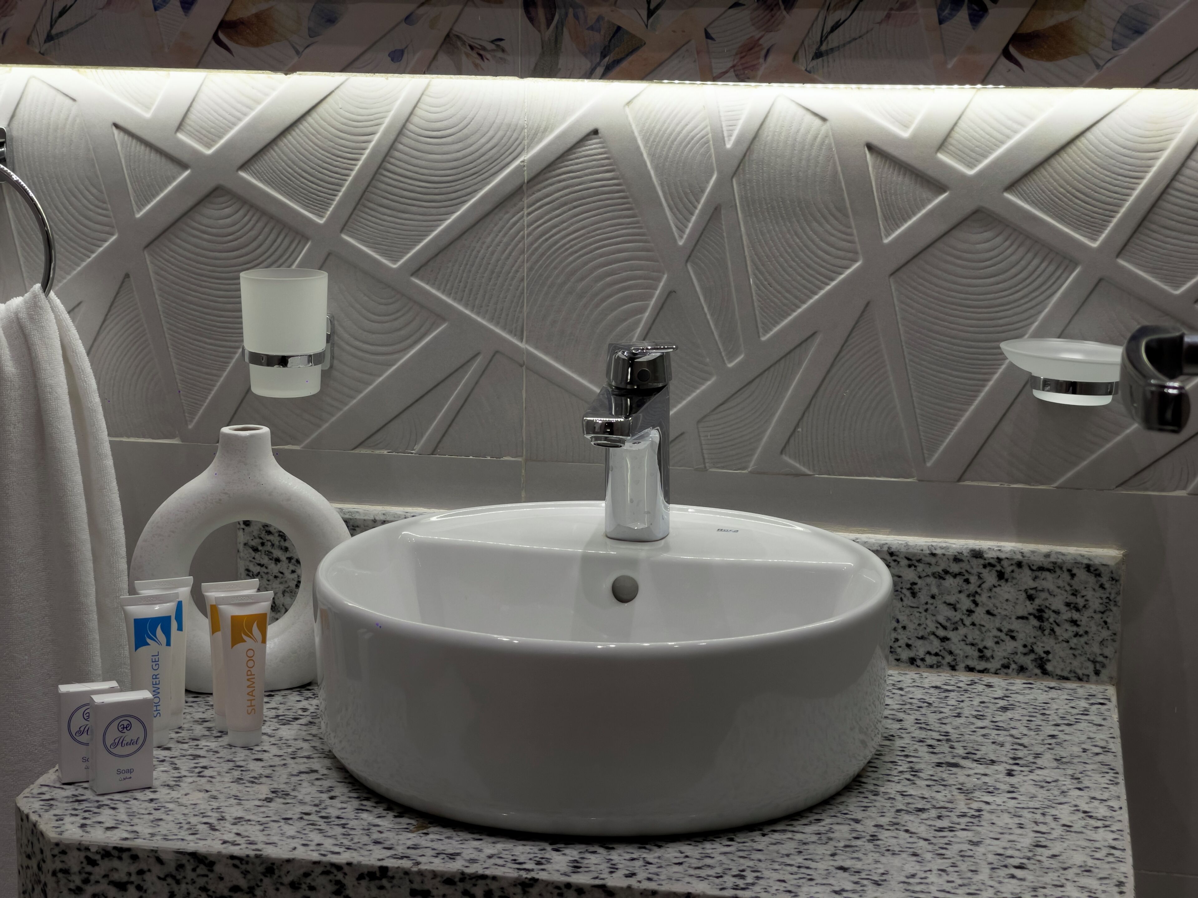 Casa de banho com uma pia redonda, uma toalha e produtos de higiene numa bancada com manchas.