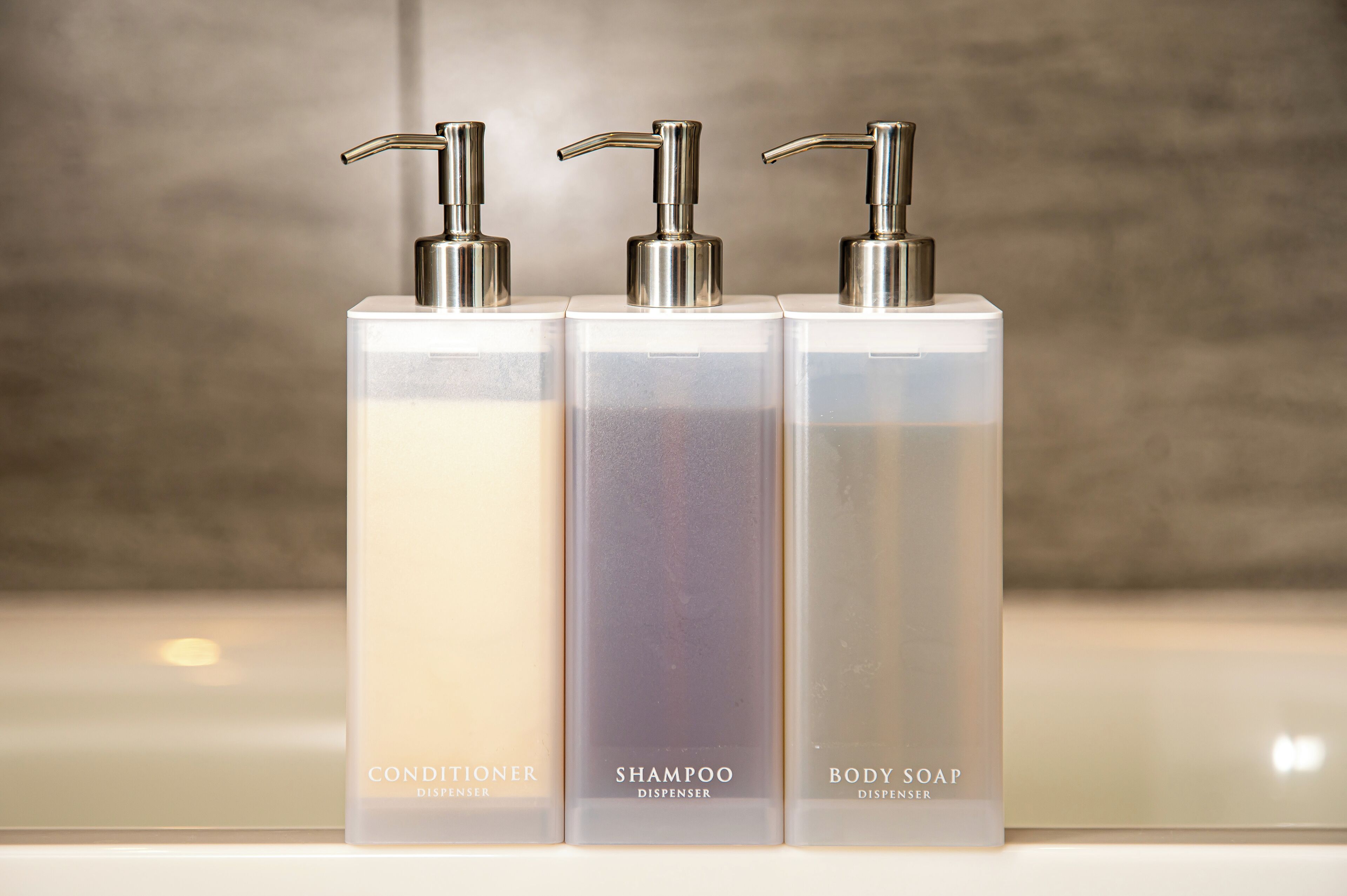 Três dispensadores de condicionador, shampoo e sabonete líquido.