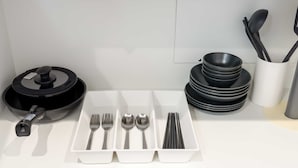 Uma bancada de cozinha com uma frigideira preta, um suporte branco com talheres e tigelas pretas empilhadas.