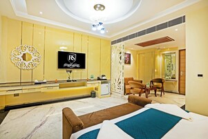 Quarto de hotel com cama, escrivaninha, cadeira, televisão e um objeto decorativo na parede.