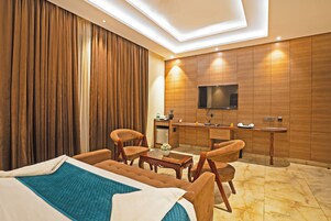 Quarto de hotel moderno com uma cama grande, área de estar com cadeiras, pequena escrivaninha, televisão de tela plana na parede e minibar.