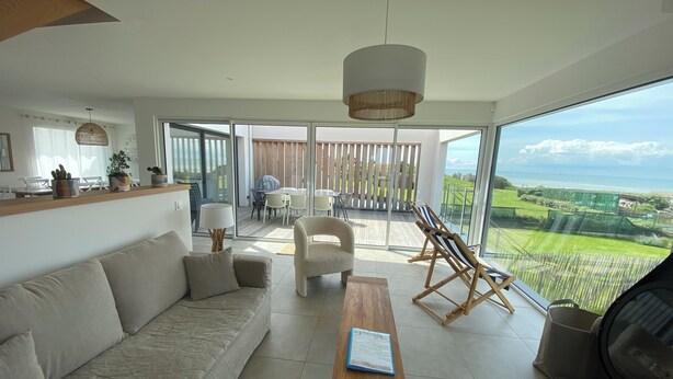 Uma sala de estar moderna com sofá, mesa de centro e vista para uma varanda com mobiliário de exterior.