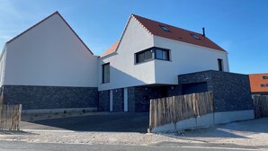Uma casa moderna de dois andares com telhado inclinado, uma pequena varanda e uma garagem.