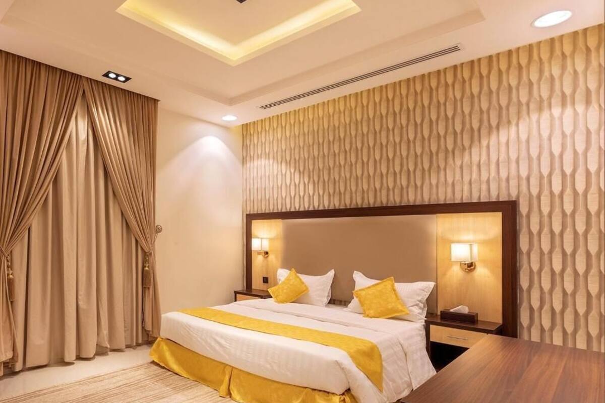 Quarto de hotel moderno com uma cama grande, cabeceira de madeira e parede estampada.