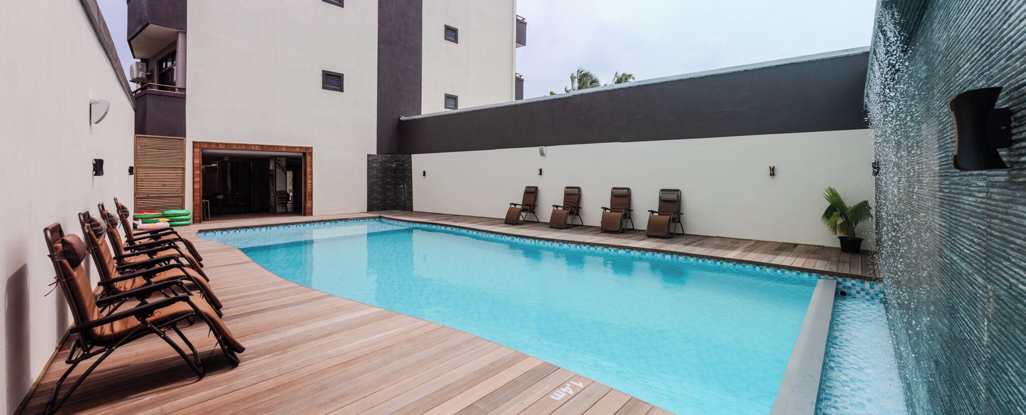 Piscina com espreguiçadeiras de madeira, pequena entrada e planta em vaso.
