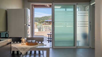 Quarto com mesa, cadeiras e porta de vidro deslizante para uma varanda com vista para uma paisagem verde.