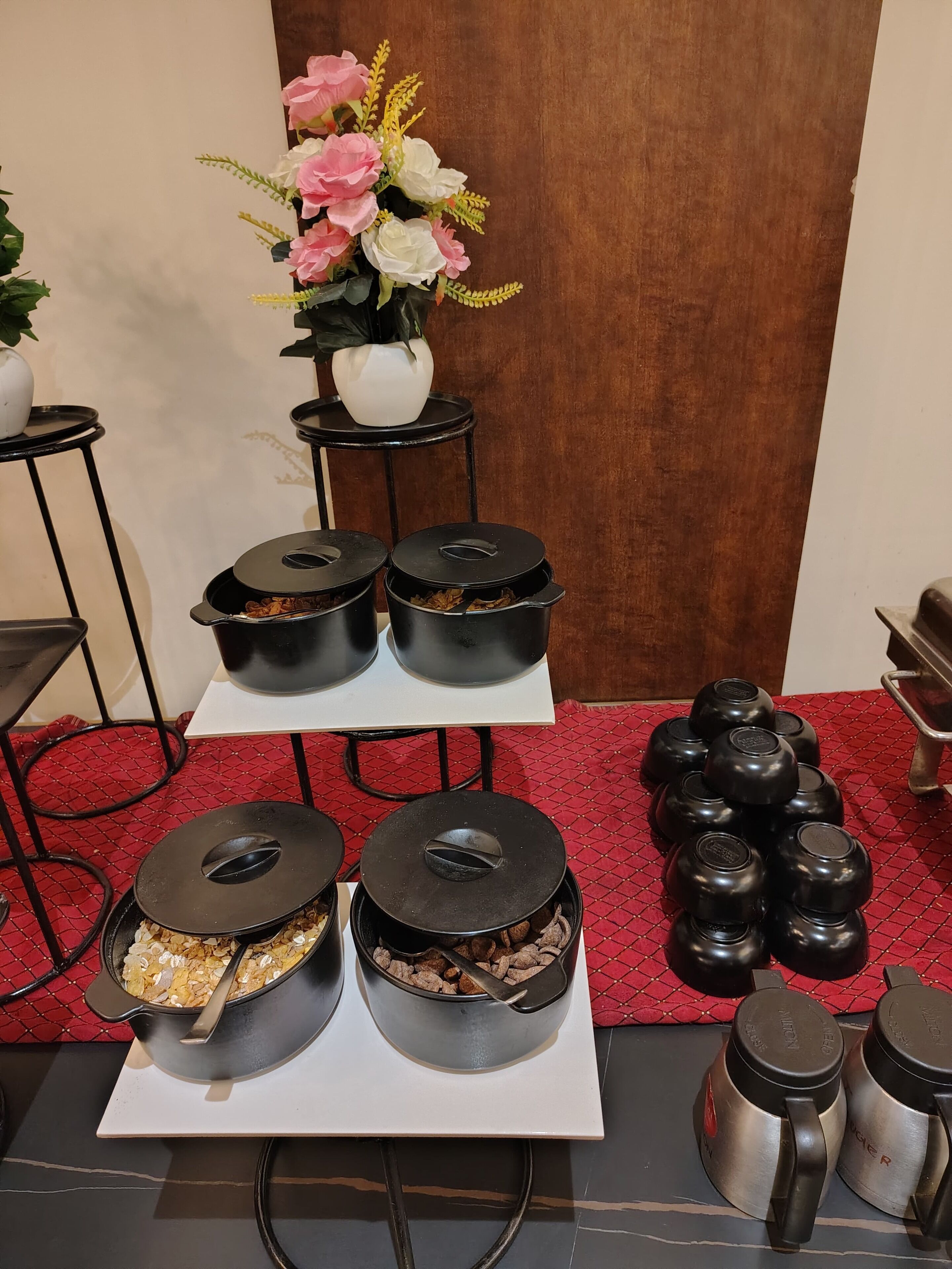 Uma cozinha com panelas em uma bancada branca, um vaso com flores sobre uma mesinha e uma toalha de mesa estampada em vermelho.