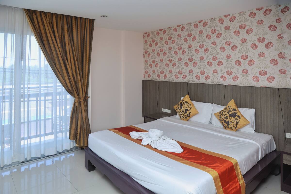 Quarto de hotel com uma cama grande, cabeceira de madeira e papel de parede estampado com flores.