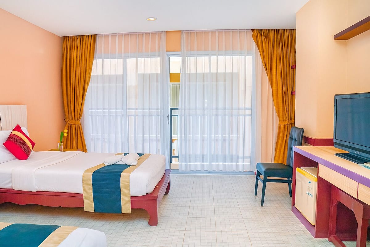 Quarto de hotel com cama, escrivaninha com televisão e vista através de grandes janelas.