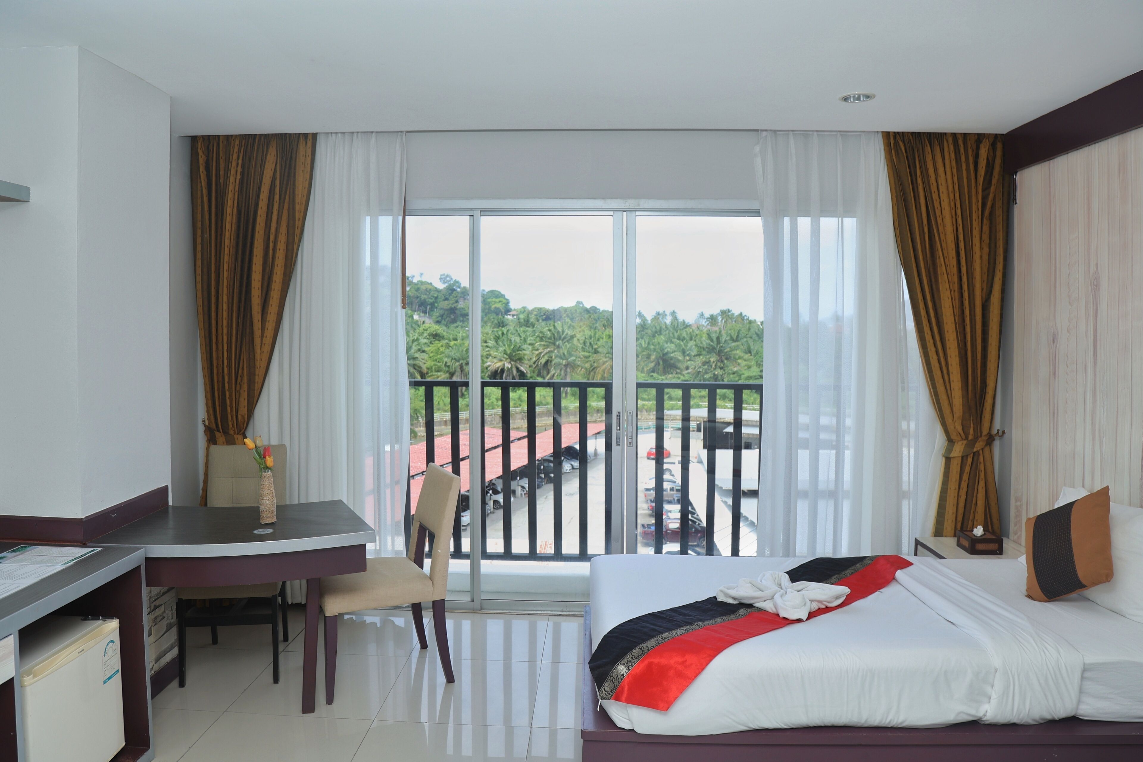 Quarto de hotel com cama, escrivaninha e cadeira. Possui uma varanda com vista para o verde.