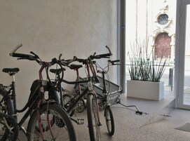 Bicicletas estacionadas em um espaço interno, com um vaso de planta e a entrada de um edifício ao fundo.