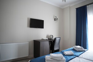 Quarto de hotel com cama, escrivaninha, cadeira, televisão de tela plana e radiador.
