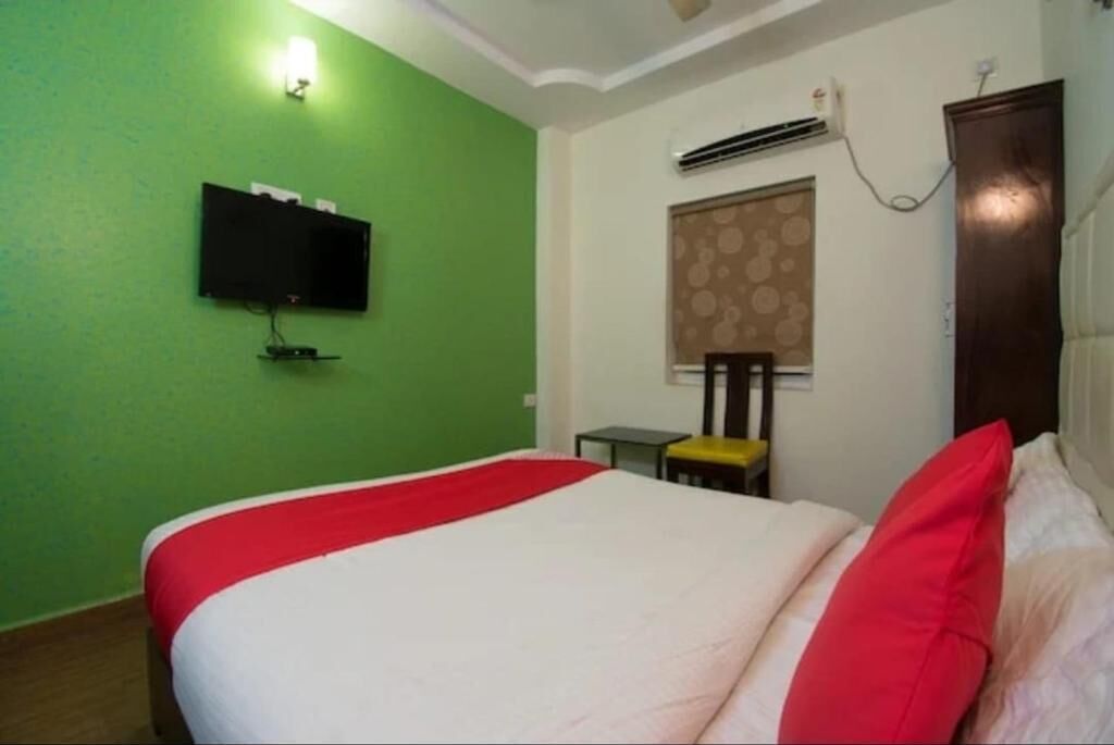 Quarto com uma cama, televisão fixada na parede, janela com persiana estampada e aparelho de ar condicionado.