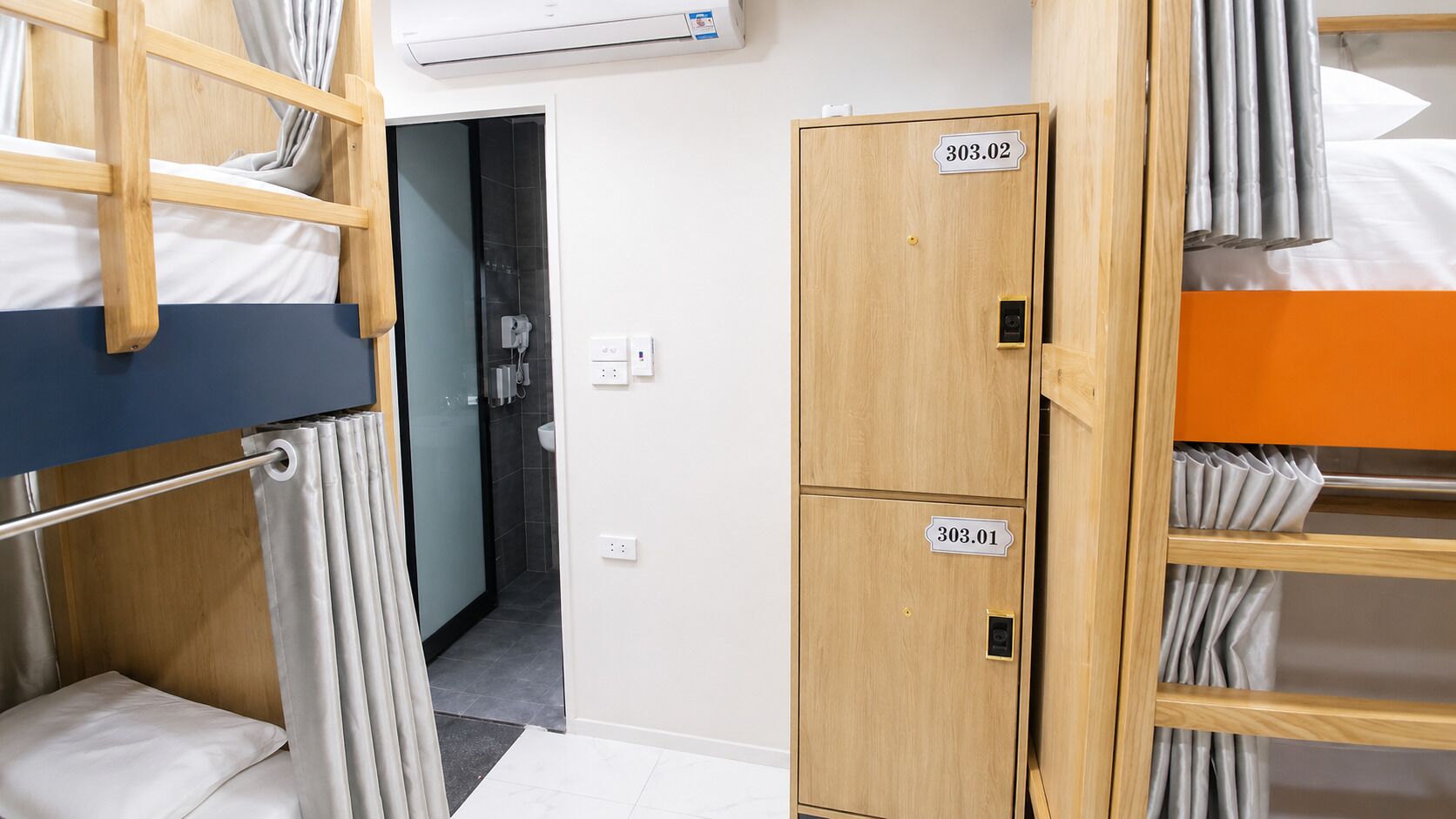 Quarto com beliche, guarda-roupa de madeira e banheiro visível através de uma porta.
