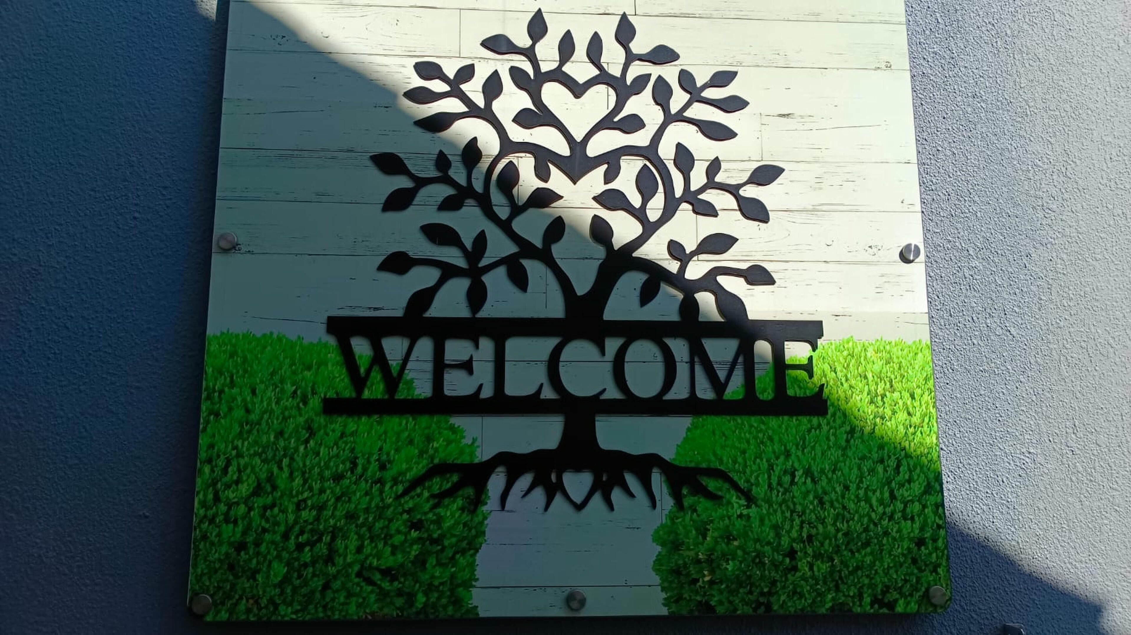 Uma placa de madeira com desenho de árvore e a palavra 'WELCOME' ao centro.