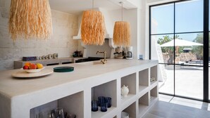 Cozinha moderna com uma ilha grande, luminárias trançadas suspensas e vista para o exterior por amplas janelas.