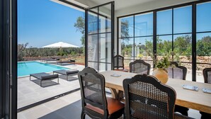 Uma área moderna para refeições ao ar livre com piscina, janelas amplas e vista para a paisagem circundante.