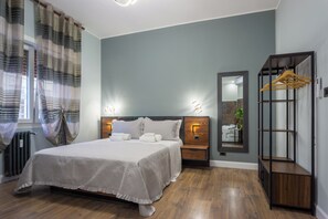 Quarto com cama grande, abajures, mesa de cabeceira de madeira, espelho e prateleira de madeira para pendurar roupas.
