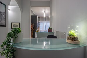 Uma receção com bancada de vidro, uma planta em vaso e quadros nas paredes.