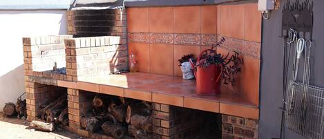 Área de churrasco ao ar livre com tijolos, painel de azulejos, churrasqueira de metal e um vaso com planta.