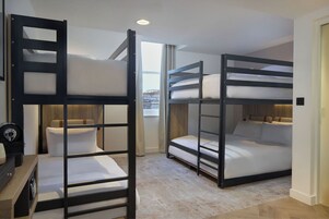 Quarto de hotel compacto com beliches, um pequeno espaço para sentar e vista pela janela.