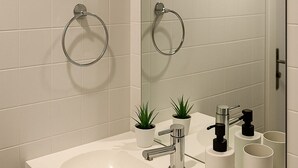 Um banheiro com pia branca, dois porta-toalhas redondos, um espelho, uma torneira, um dosador de sabonete e duas plantas em vasos.