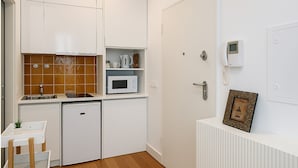 Uma cozinha compacta com armários brancos, micro-ondas, pia e um refrigerador pequeno.