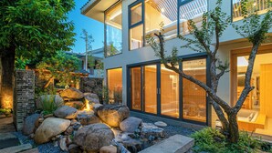 Uma casa moderna com jardim de pedra, um elemento de cascata e uma grande porta de vidro que dá para uma sala de estar.