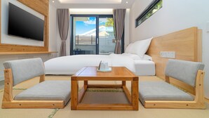 Quarto de hotel moderno com uma cama grande, uma mesa de centro de madeira, duas poltronas estofadas, uma TV de tela plana na parede e uma porta de vidro deslizante que dá para uma varanda.